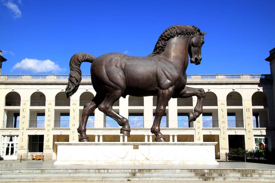 Uma estátua de bronze de um cavalo em frente a um edifício com janelas e colunas em arco.