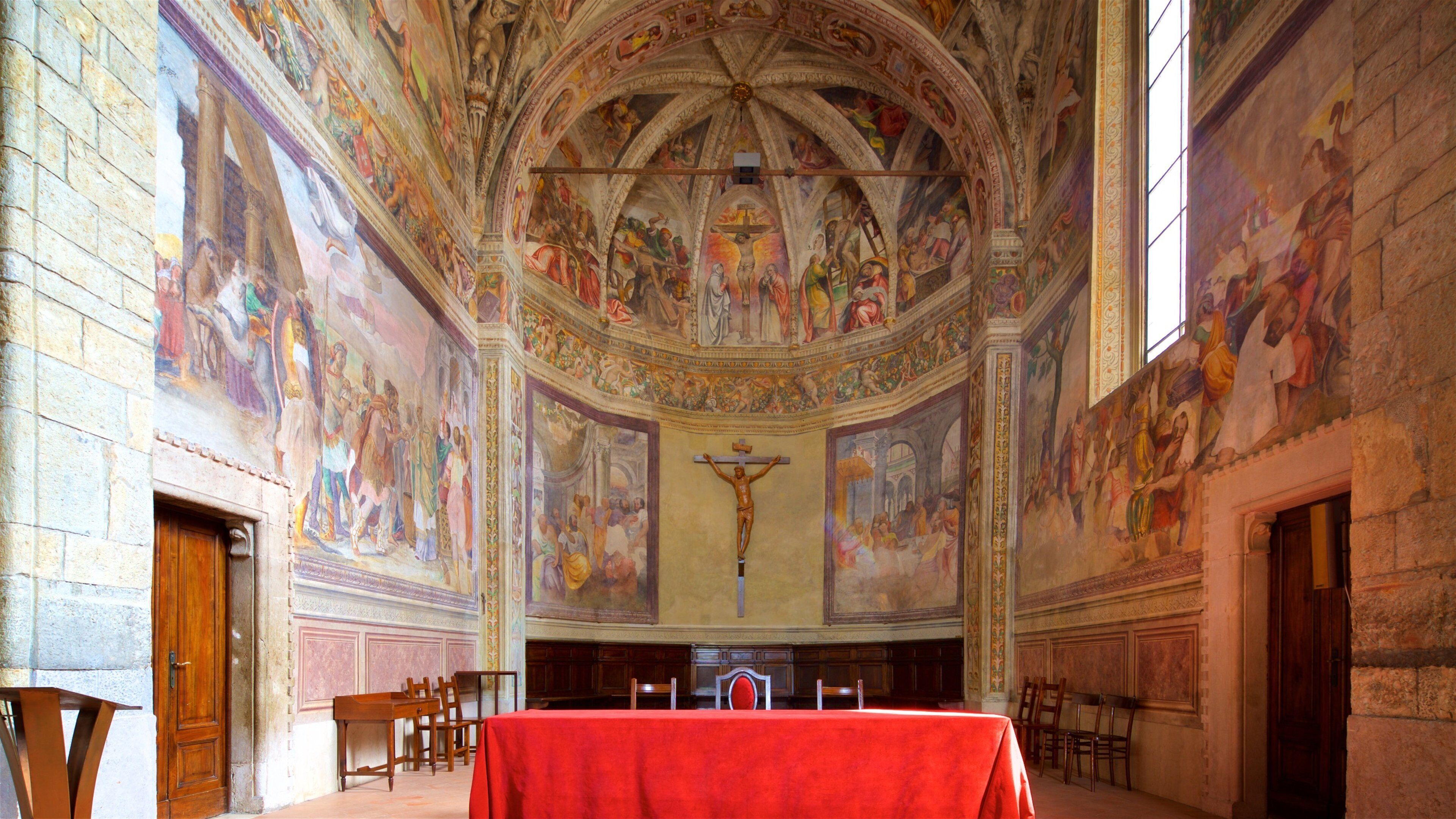 Interior com altar vermelho, afrescos e uma cruz.