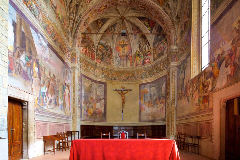 Interior com altar vermelho, afrescos e uma cruz.