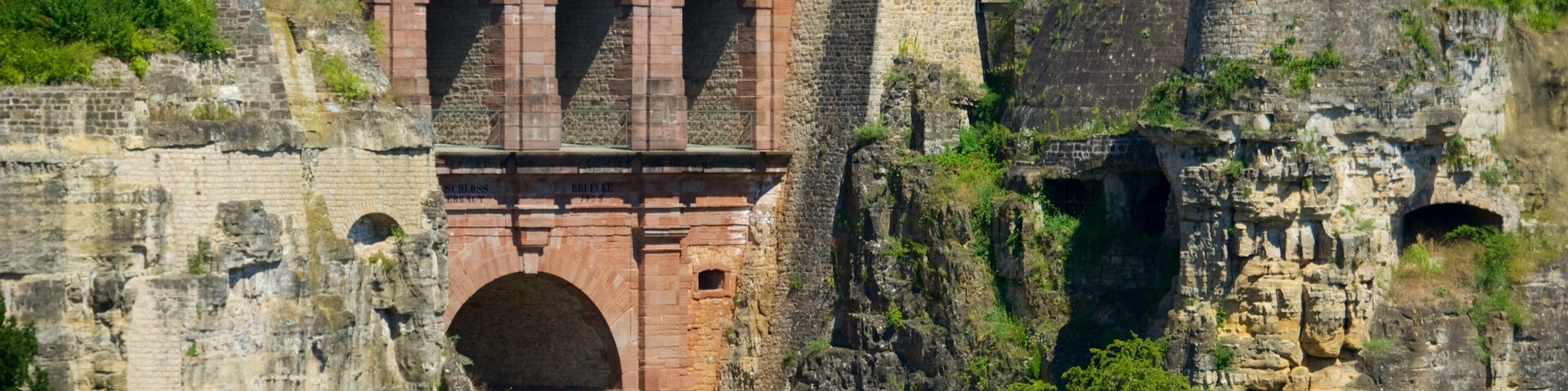 Uma ponte de pedra histórica com arcos, um muro de pedra e um caminho.
