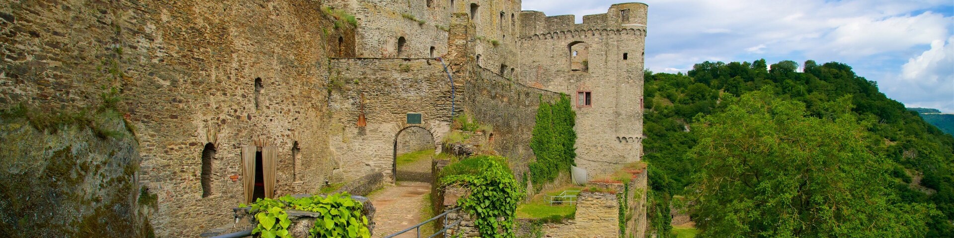 Um castelo de pedra histórico com uma colina íngreme e coberta de relva ao fundo.