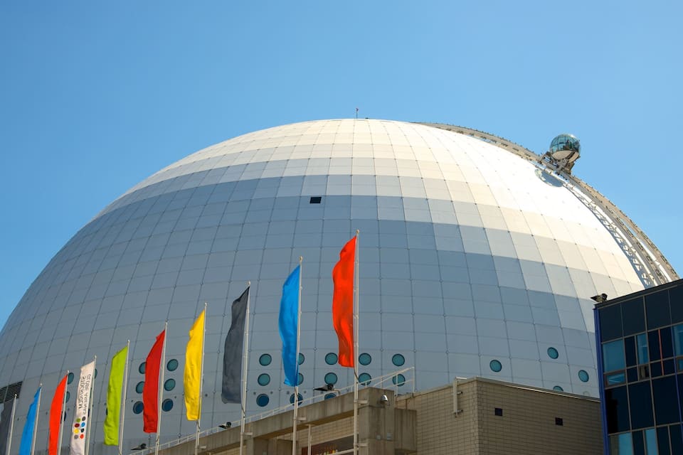 Um edifício em forma de cúpula grande, com várias bandeiras coloridas e uma antena parabólica no topo.