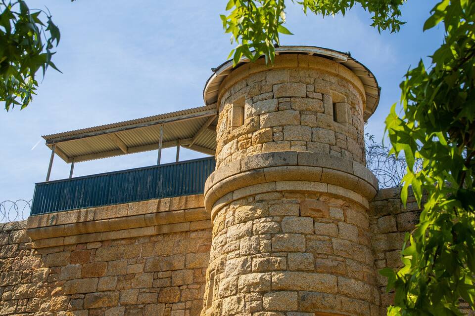 Uma torre de pedra com telhado de metal, rodeada por vegetação.