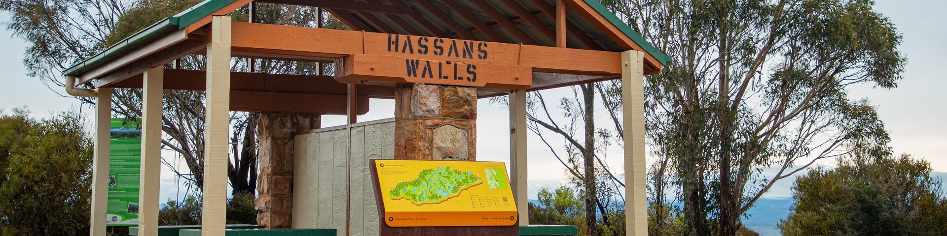 Uma estrutura de madeira identificada como 'Hassans Walls', com uma placa de mapa e um banco.