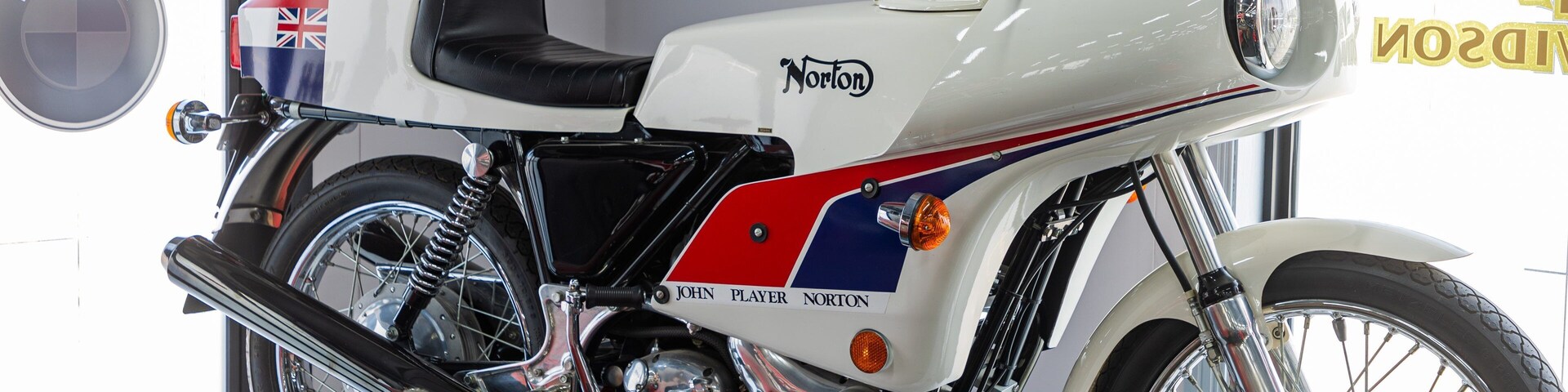 Uma moto Norton antiga em exposição, com uma placa que descreve sua história.