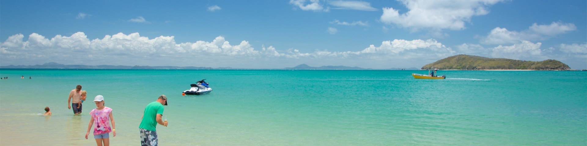 Uma praia com águas turquesa cristalinas, um jet ski e uma ilha ao longe.