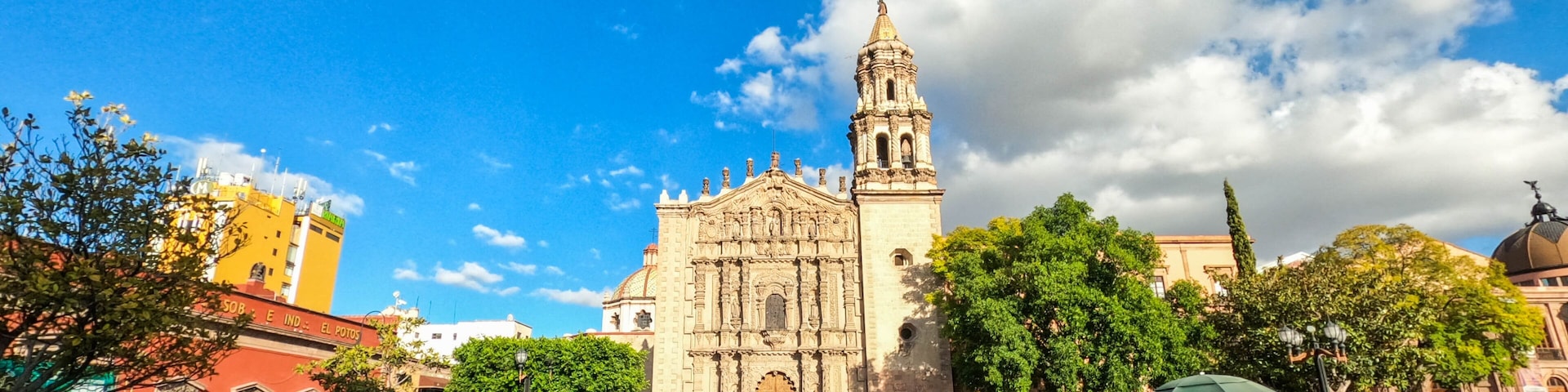 Uma igreja histórica com um campanário, rodeada por uma praça com pessoas e coloridas bancas de mercado.