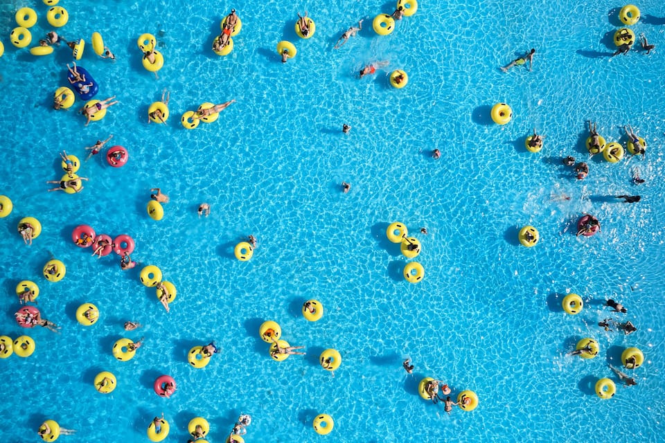 Pessoas flutuando em bóias amarelas e vermelhas em uma piscina.