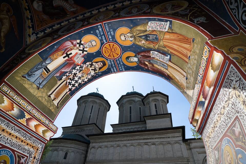 Um mural detalhado com figuras e símbolos religiosos, uma estrutura em cúpula e um céu azul límpido.