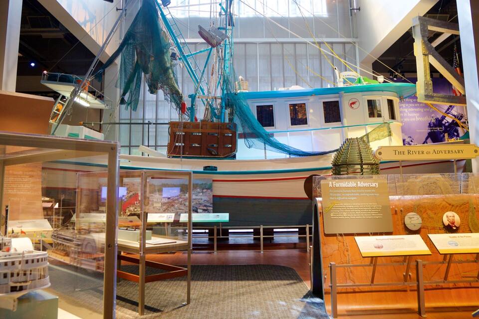 Exposição em museu com um modelo de barco a vapor, rede e placa que diz "O Rio como Adversário".