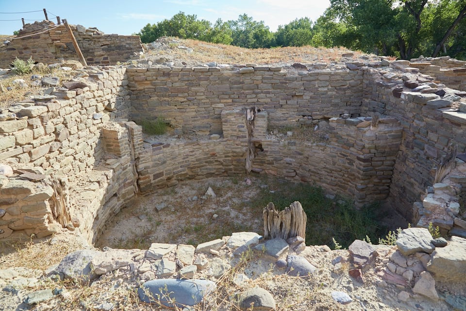 Estrutura de pedra antiga com uma área central circular, rodeada por muros e pedras espalhadas.