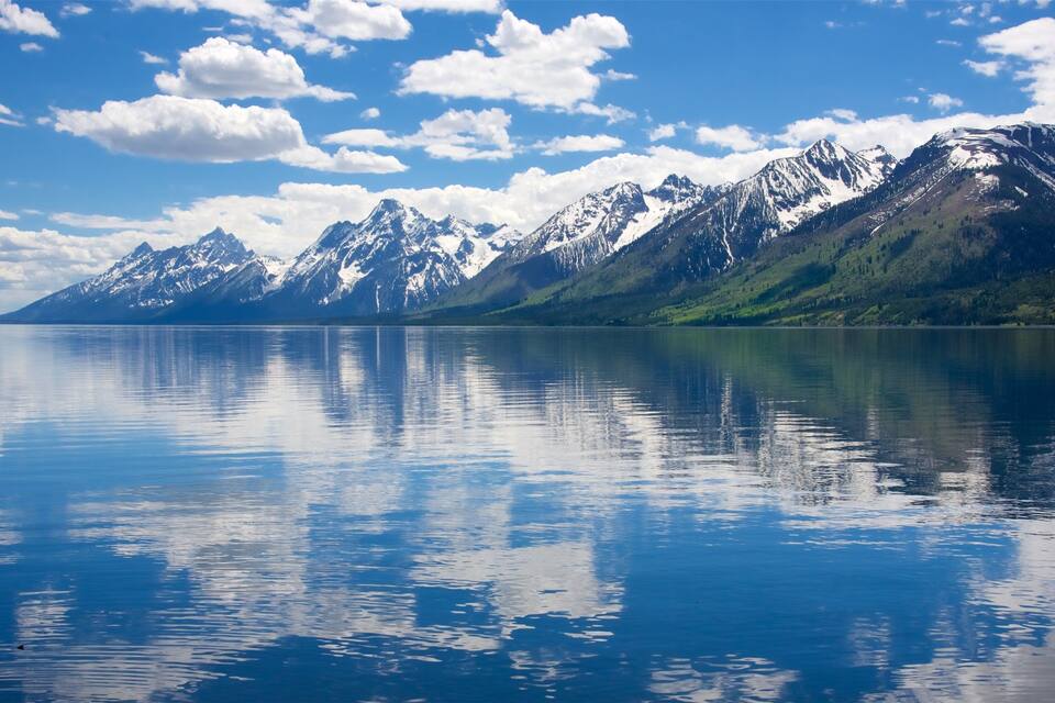 Um lago tranquilo refletindo montanhas cobertas de neve sob um céu parcialmente nublado.