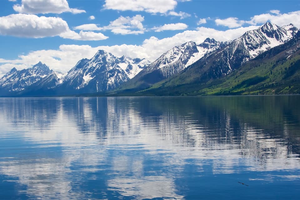 Um lago calmo refletindo montanhas cobertas de neve sob um céu límpido.