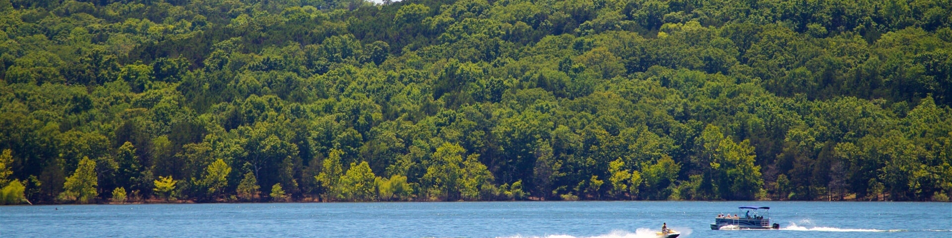 Um lago com um barco deslizando sobre a água e uma colina arborizada ao fundo.