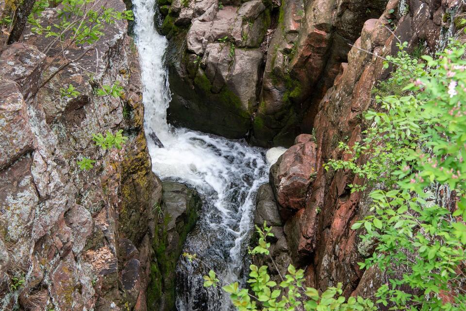 Uma cascata desce por um terreno rochoso, cercada por vegetação.
