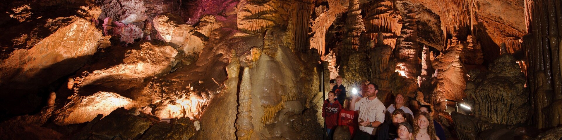Um grupo de pessoas dentro de uma caverna com estalactites e um brilho rosado.