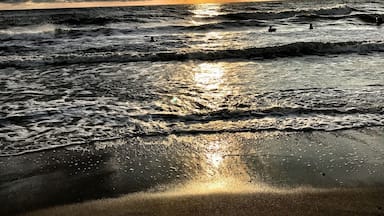 Uma praia com ondas, um pôr do sol e um céu nublado.