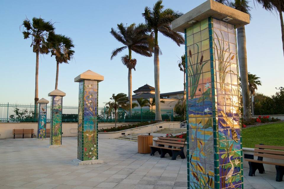 Um parque com pilares azulejados, bancos, palmeiras e um edifício ao fundo.