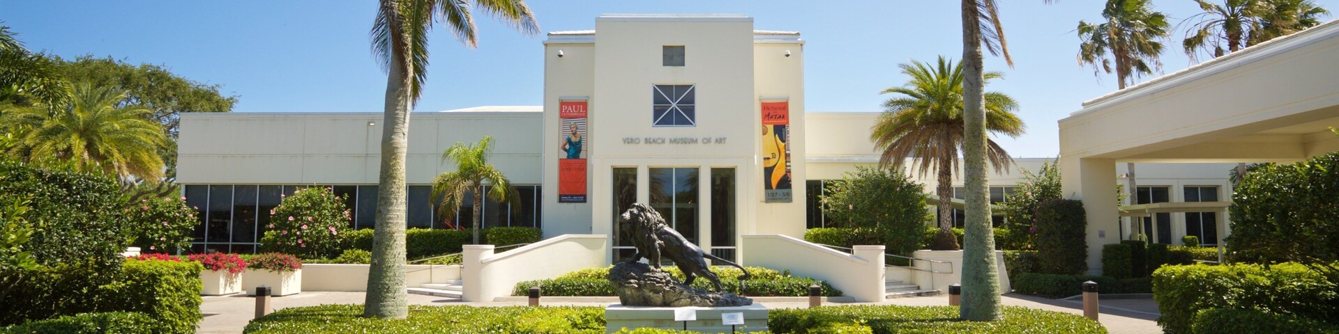 Museu de Arte de Vero Beach com uma escultura central, palmeiras e um calçadão.