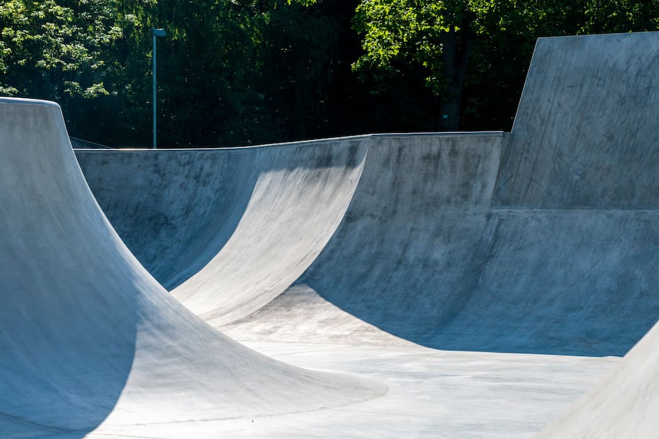 Pista de skate com várias rampas de concreto e um fundo arborizado.