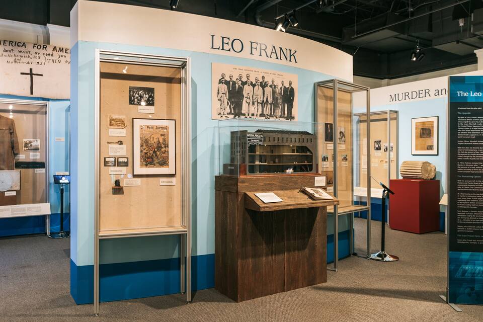 Exposição de museu sobre Leo Frank, com fotografias históricas, documentos e uma vitrine com uma maquete de um edifício.