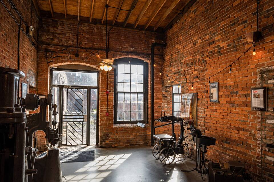 Um quarto com paredes de tijolo, uma grande janela em arco, equipamentos industriais e uma bicicleta.