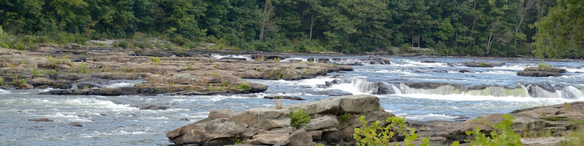 Um rio com corredeiras, cercado por pedras e vegetação.