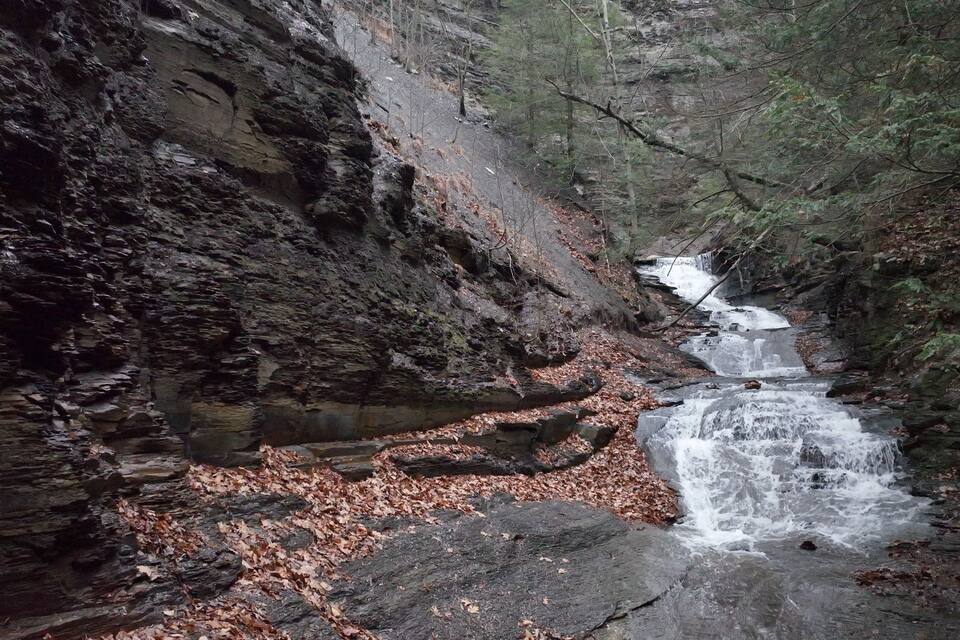 Uma cachoeira caindo sobre rochas em uma área arborizada.