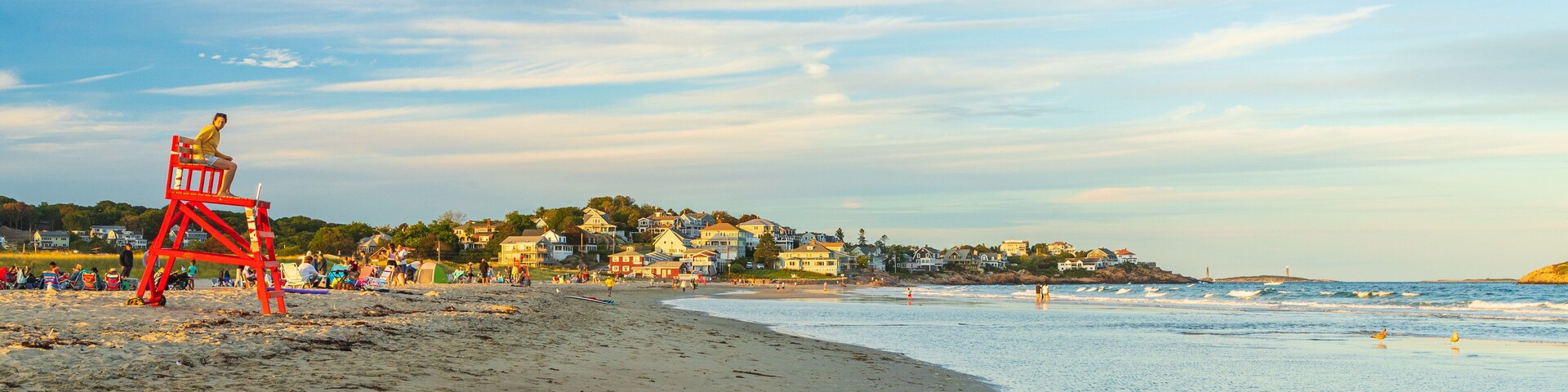Uma praia com uma torre salva-vidas, casas ao fundo e o oceano.