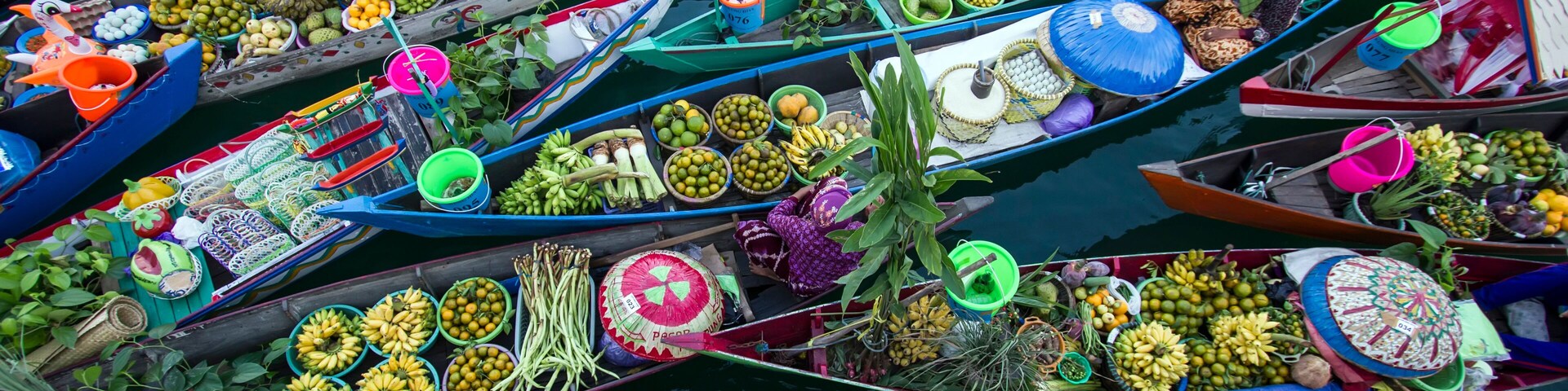 Uma frota de barcos coloridos carregados com várias frutas e legumes em um corpo d'água.