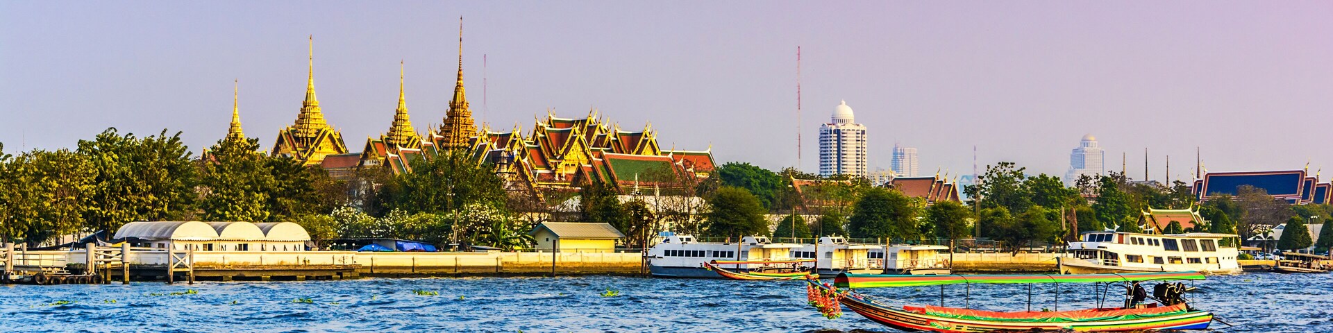 Um rio com barcos tradicionais e um templo com torres douradas.