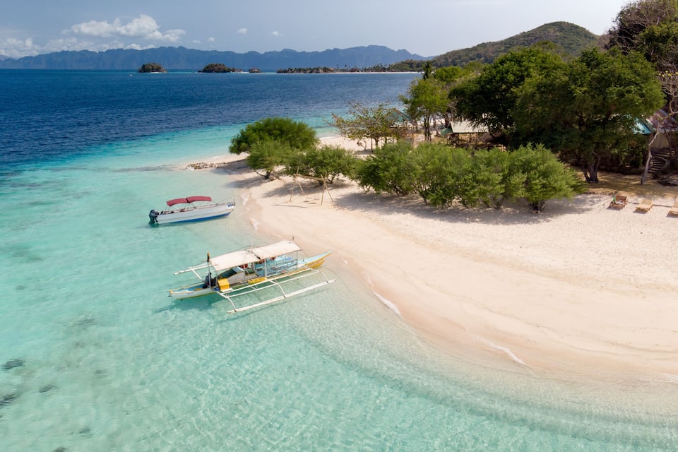 Uma praia com águas turquesa cristalinas, um barco e uma cabana pequena.
