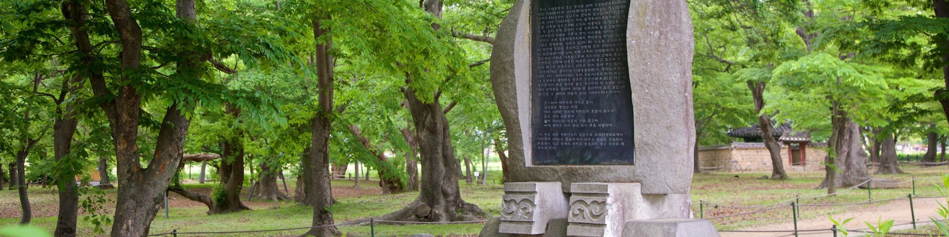 Um monumento de pedra com uma inscrição, cercado por árvores em um parque.