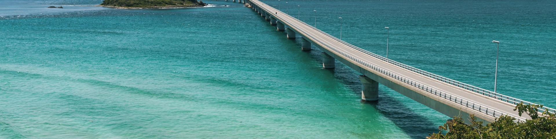 Uma longa ponte atravessa águas turquesa, com uma ilha arborizada ao fundo.