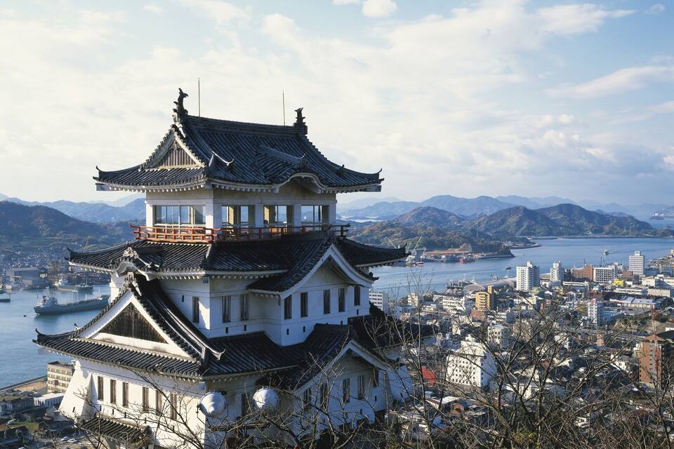 Uma pagoda japonesa tradicional com vários níveis, com vista para uma paisagem costeira e montanhas ao fundo.