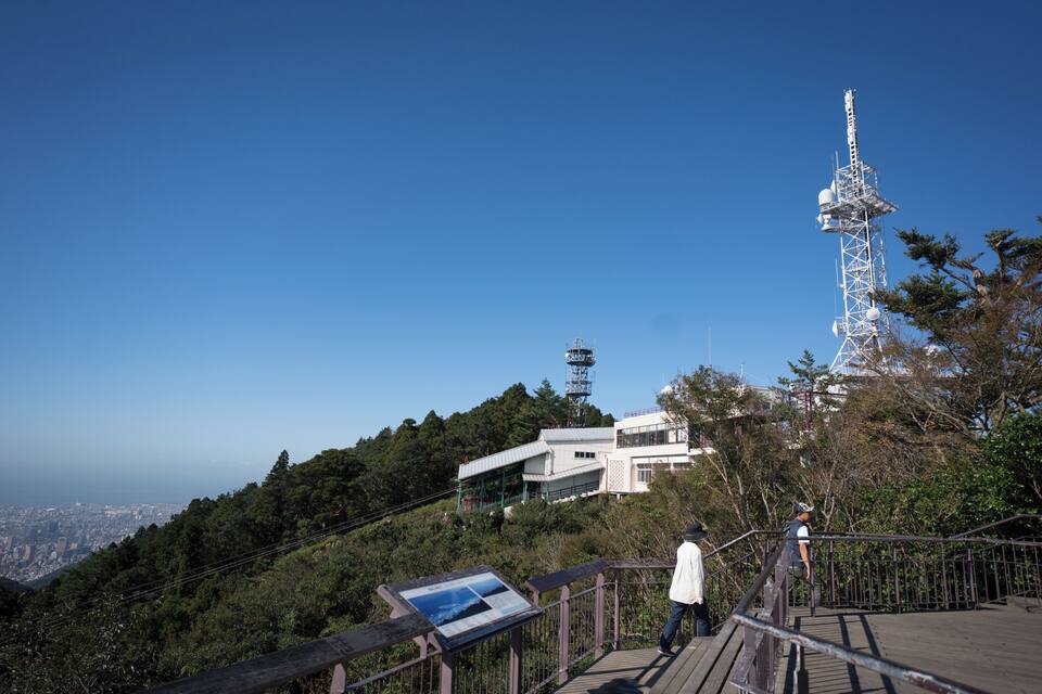 Um mirante com vista panorâmica, um edifício moderno, uma torre de comunicação alta e uma paisagem urbana ao longe.