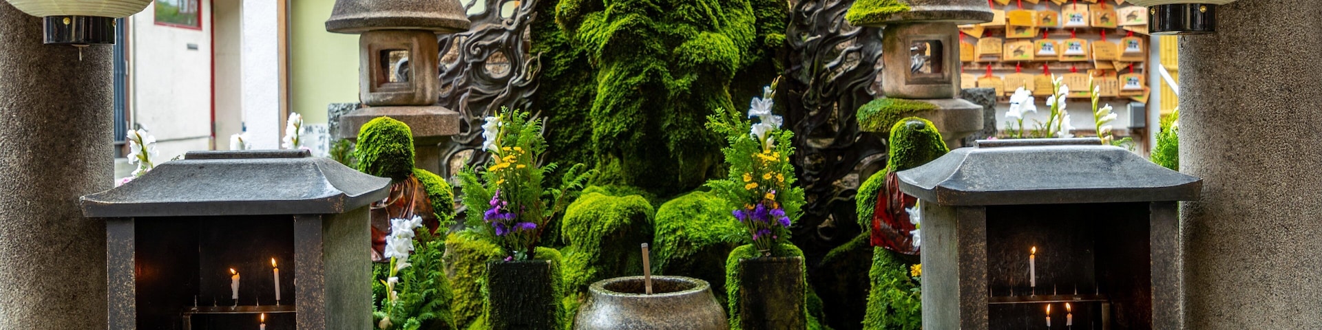 Um santuário japonês tradicional com lanternas de pedra, altar coberto de musgo e bandeiras vermelhas.
