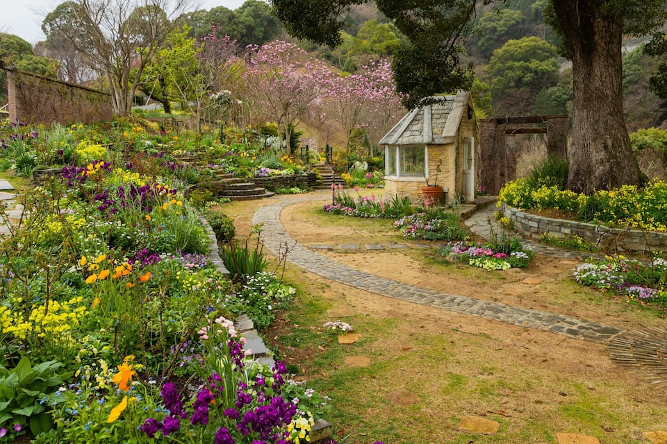 Um jardim com caminho de pedra, flores coloridas e um pequeno edifício de pedra.