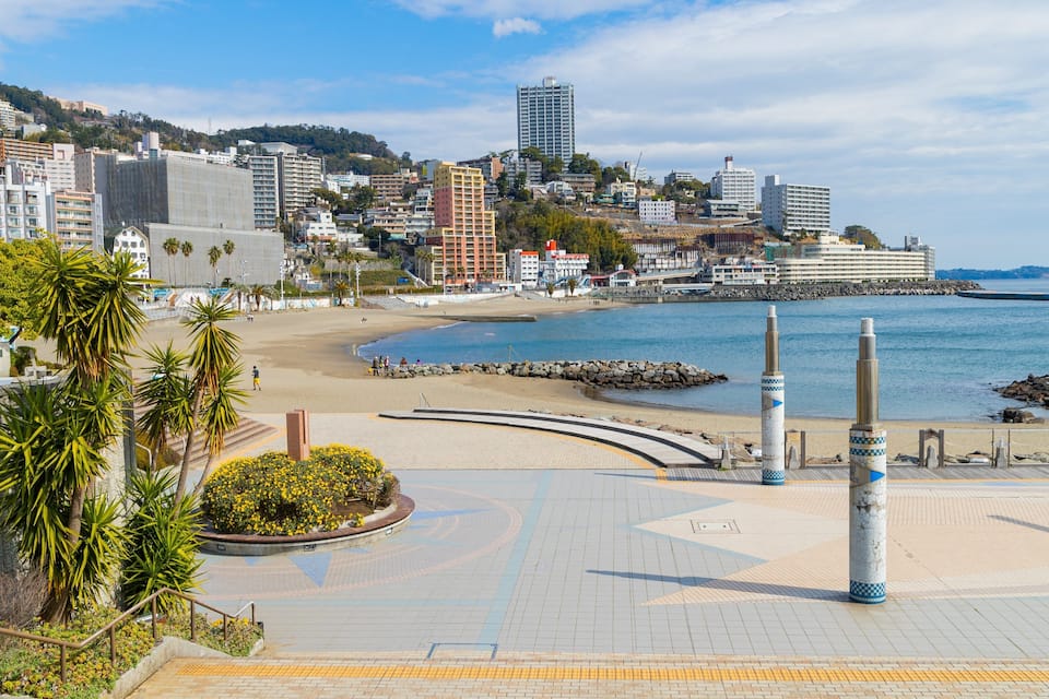 Paisagem costeira urbana com praia, palmeiras e uma mistura de edifícios modernos e tradicionais.