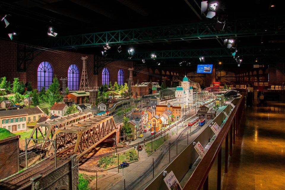 Uma maquete detalhada de trem com edifícios em miniatura, trilhos e uma torre do relógio.