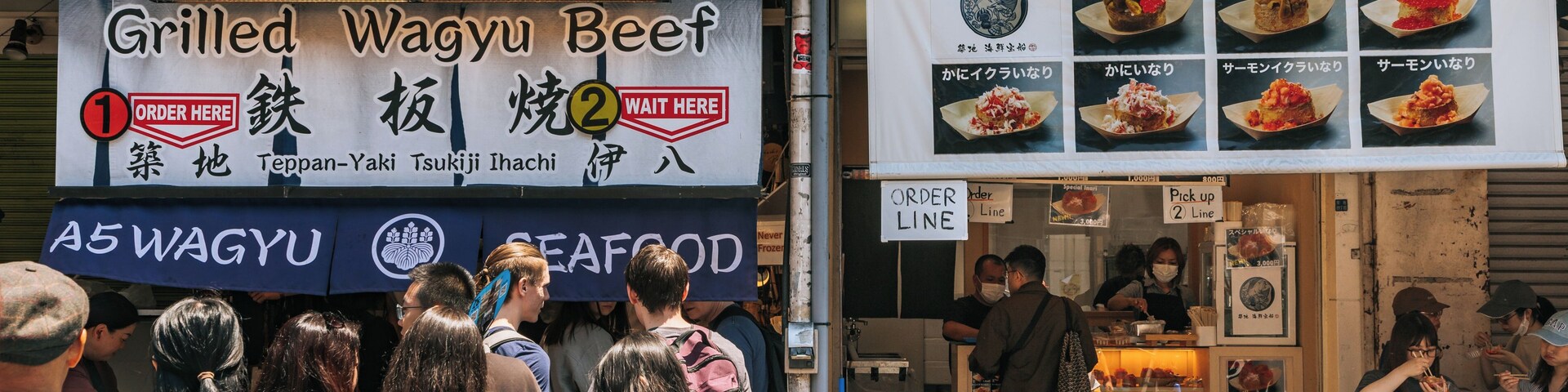 Rua movimentada com um quiosque anunciando carne wagyu grelhada e outro com takarabune.