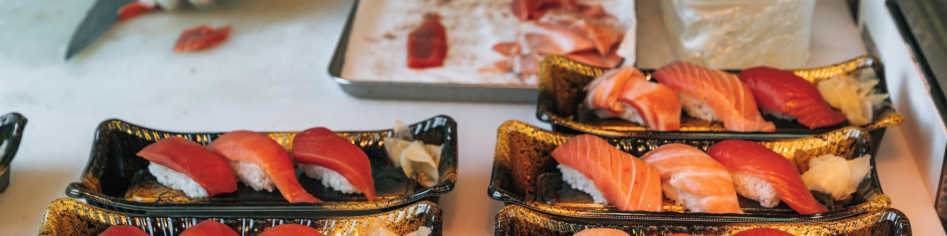 Quatro bandejas de sushi com salmão dispostas sobre uma mesa.