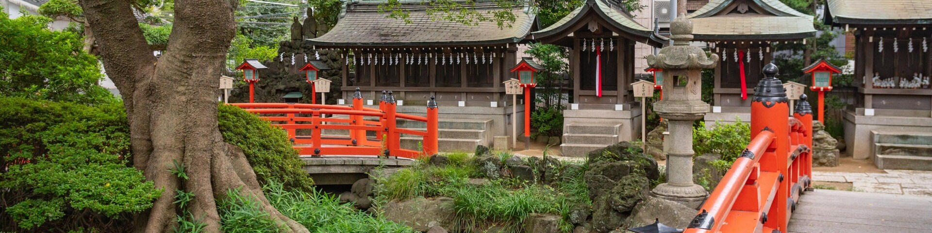 Um templo japonês tradicional com um portão torii vermelho, um candeeiro de pedra e um pequeno lago.