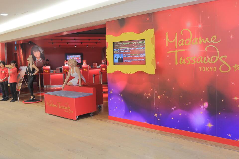 O museu de cera Madame Tussauds, com uma grande exposição de uma figura de cera e uma placa com a inscrição 'Madame Tussauds Tóquio'.