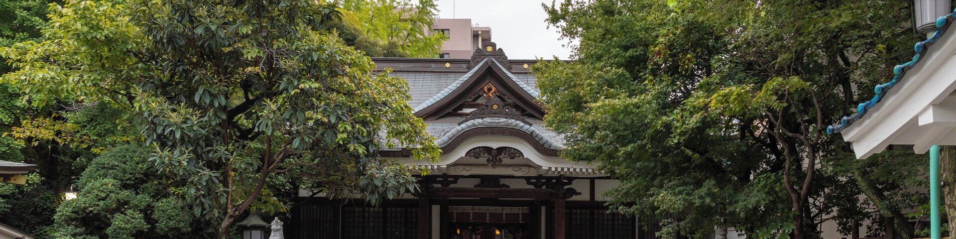 Um templo japonês tradicional com um portão de madeira, lanternas de pedra e uma estátua de lobo.