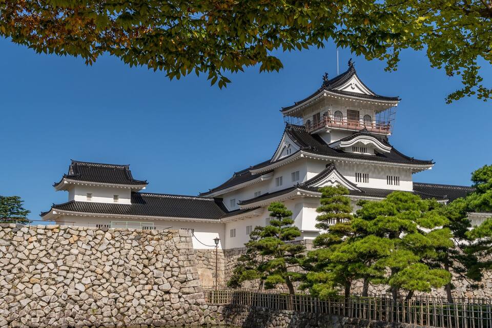 Um castelo japonês tradicional com muralha de pedra e vegetação exuberante.