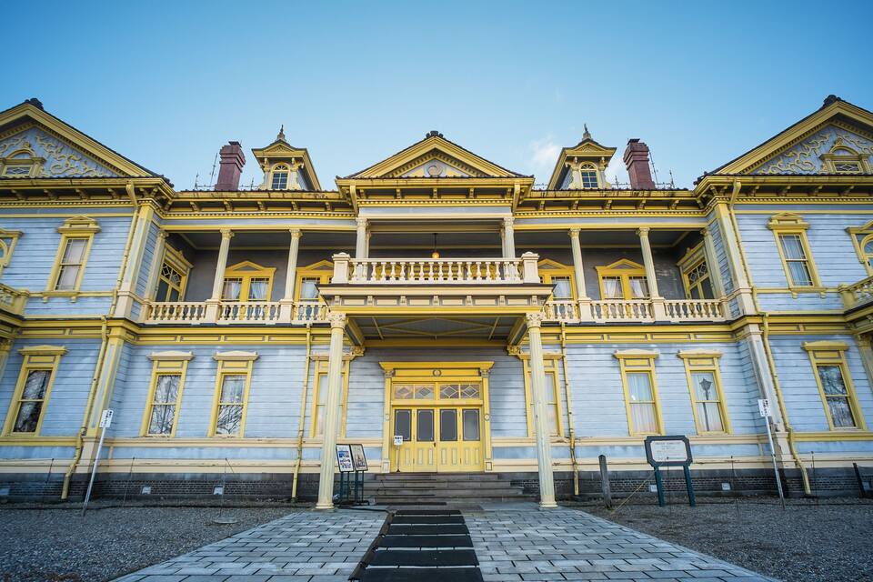 Um edifício grande e ornamentado com detalhes em amarelo e azul, uma varanda central e uma fachada simétrica.