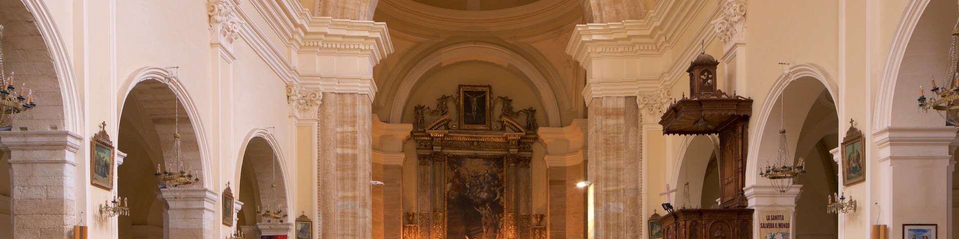 Interior de uma igreja com tetos em arco, bancos de madeira e um altar central com estátuas religiosas e velas.