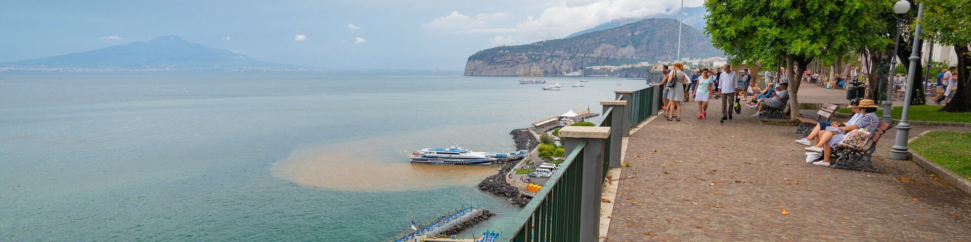 Um calçadão à beira-mar com vista clara para o oceano, um cais e barcos.