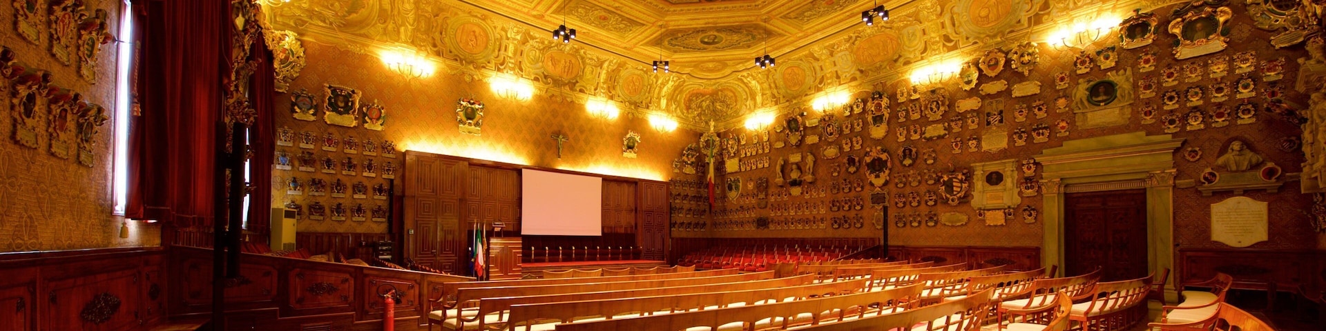 Um teatro ornamentado com teto dourado, fileiras de cadeiras de madeira e um palco com tela de projeção.